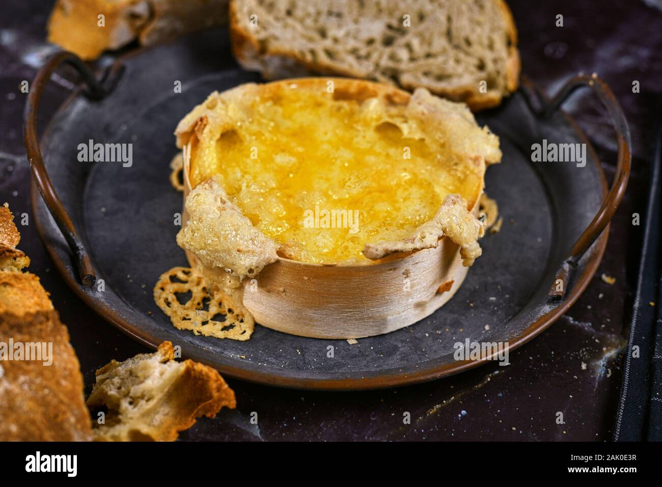 Baked and melted oven cheese in round wooden tray with fresh bread ...
