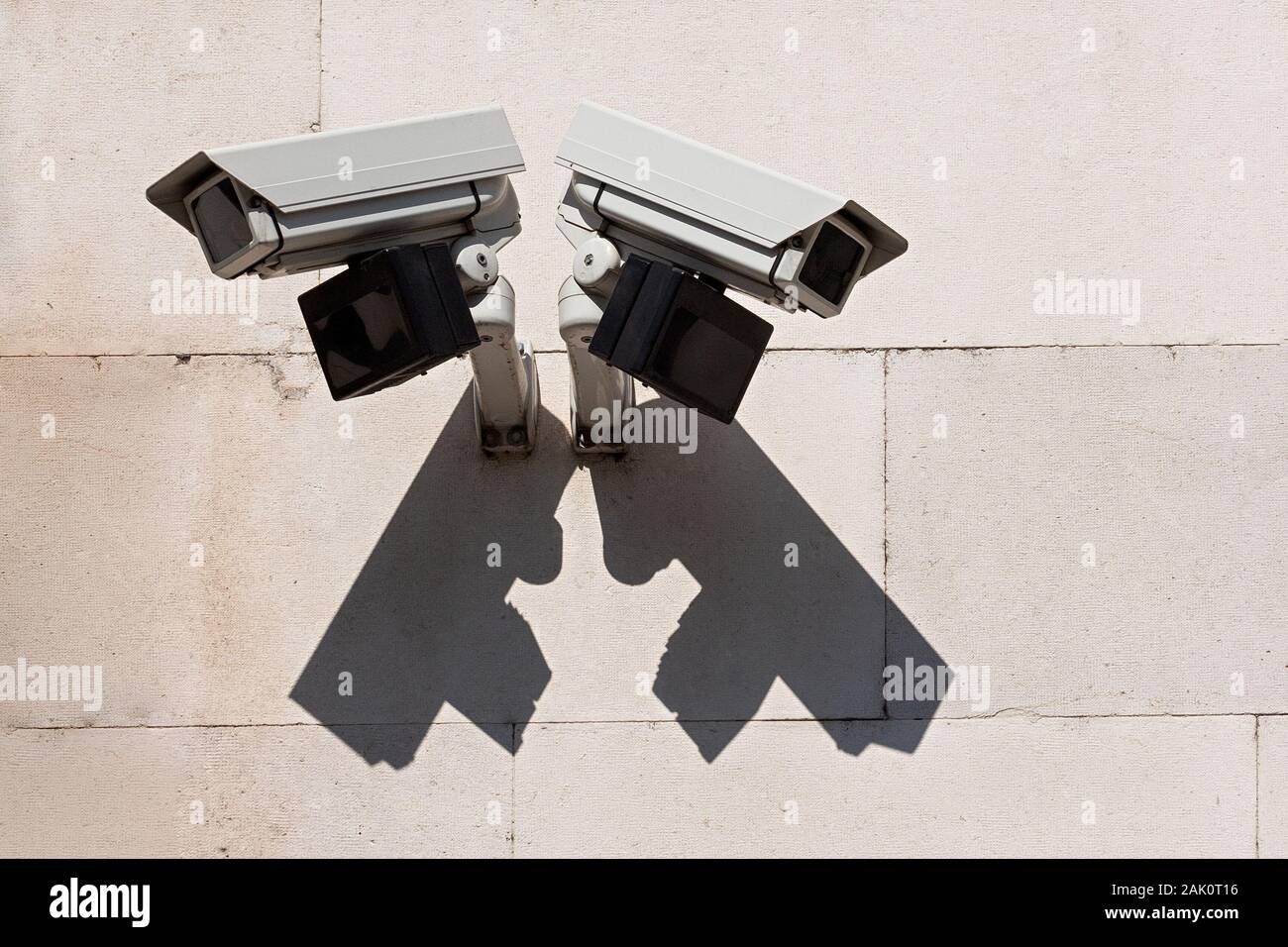 Two surveillance cameras on the white wall in the sunlight, casting ...