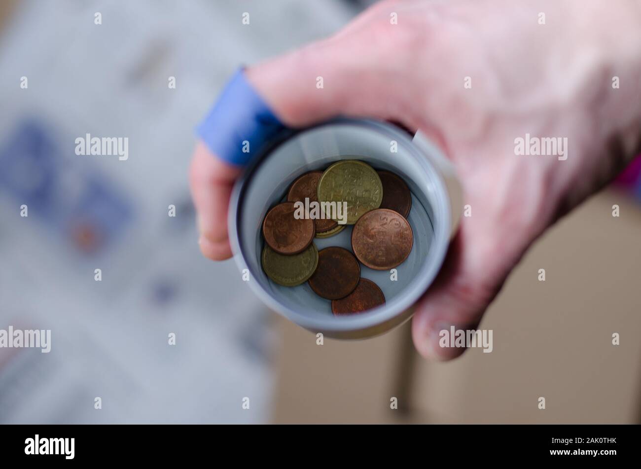 A person holding a cup with some coins begging for more change Stock ...