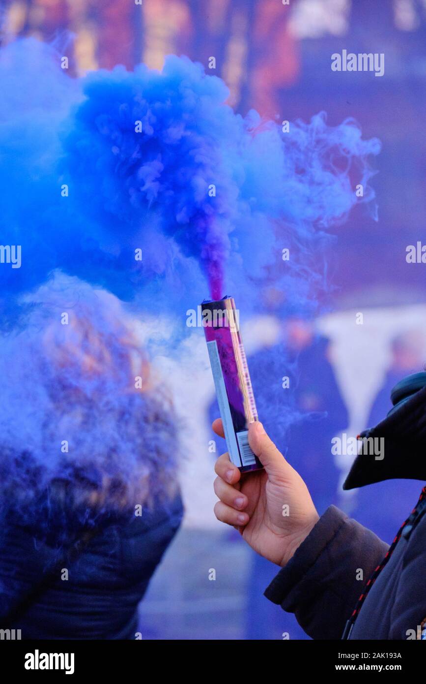 The hand holds a fireworks with a smoke of the color of blue in a crowd ...