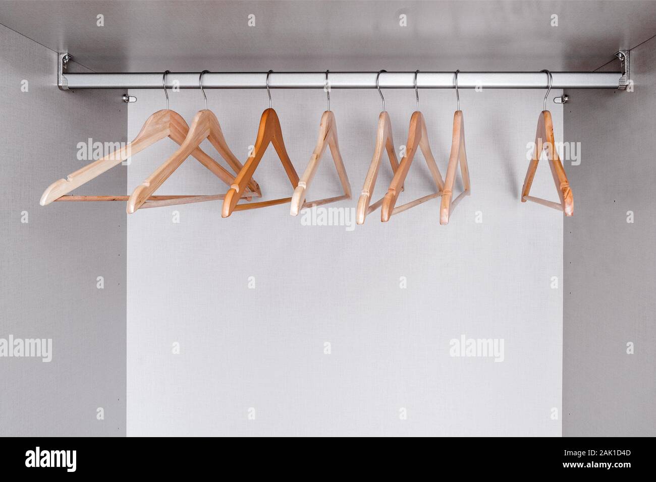 Empty, lacquered light wood clothes hangers hang in wardrobe on metal ...