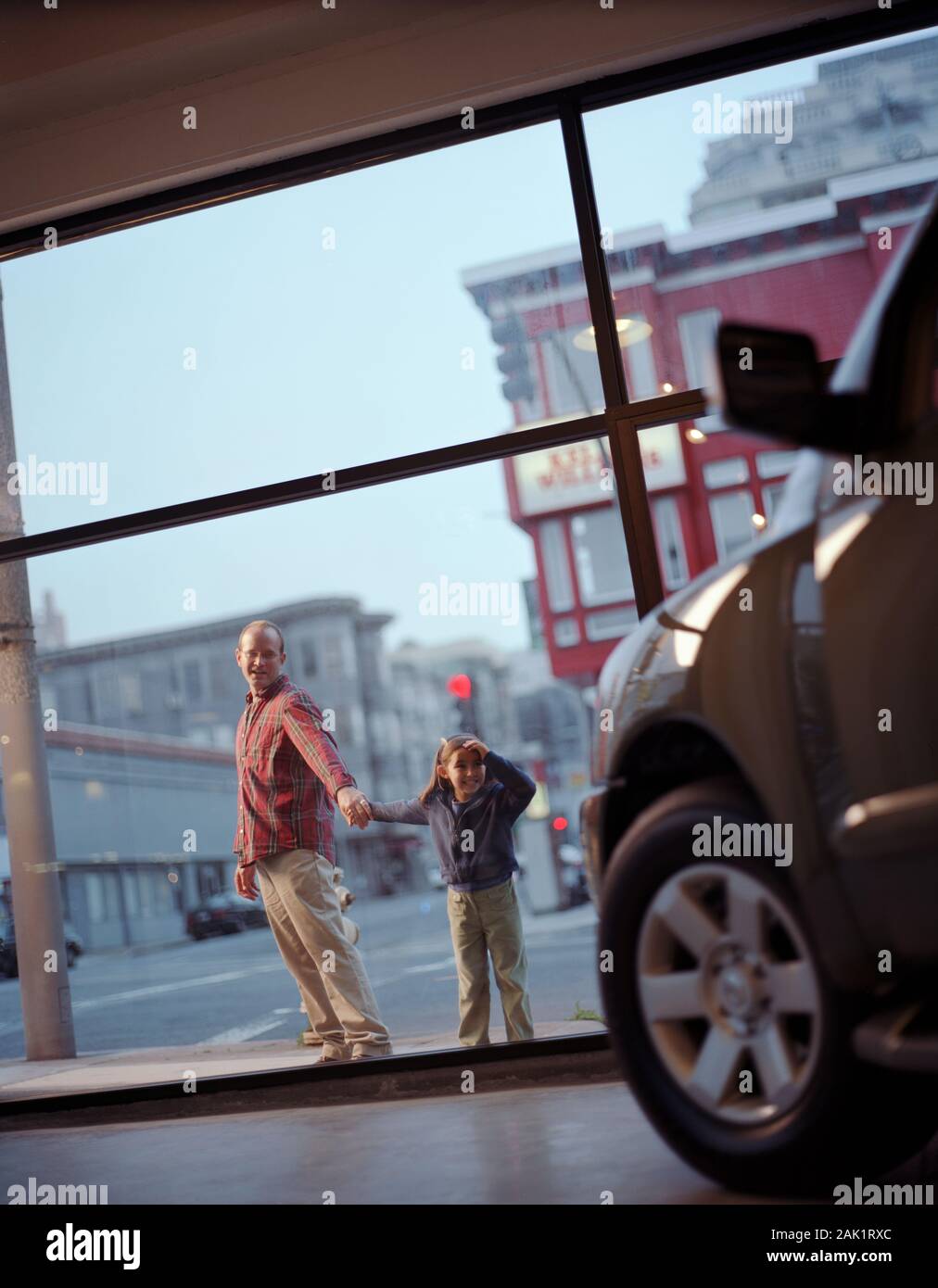 Young girl and her father looking through a large window at a new car ...