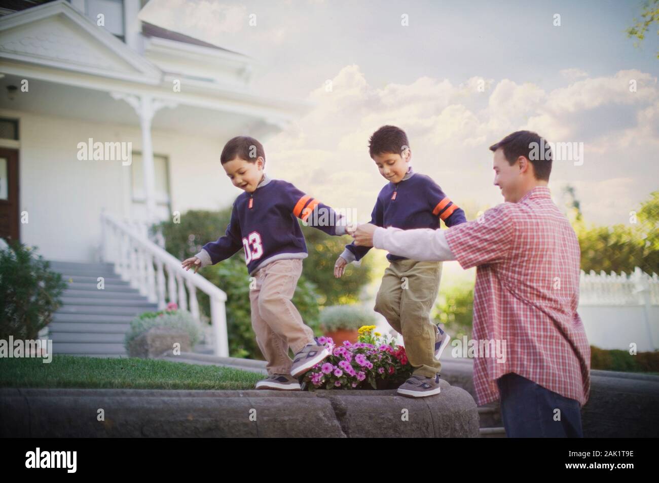father helps two sons walk along ledge Stock Photo - Alamy