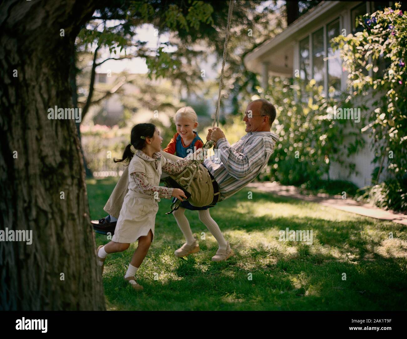 two girls pushing man on swing Stock Photo - Alamy