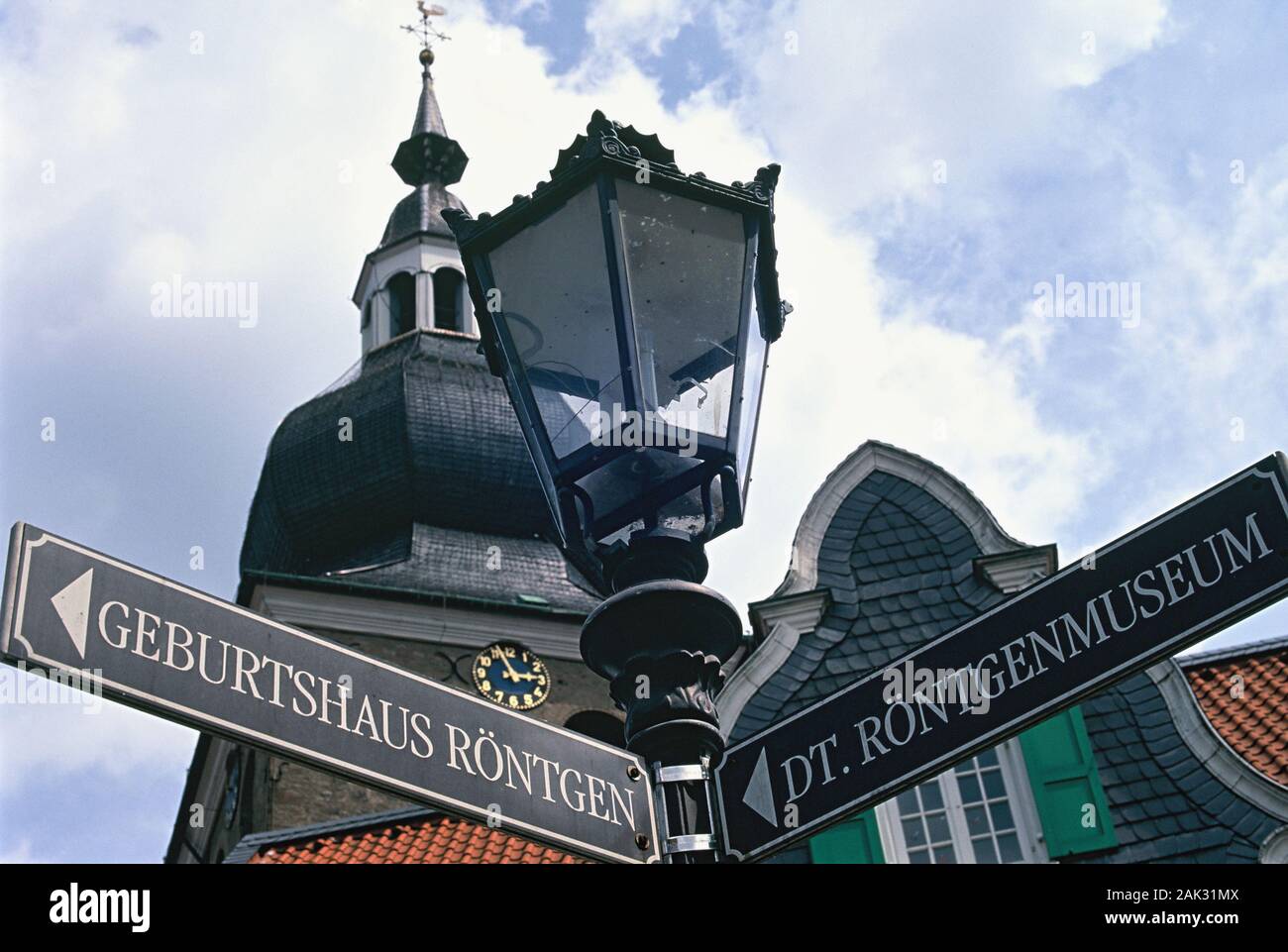 The picture shows a steeple and in front a street lamp with two road ...