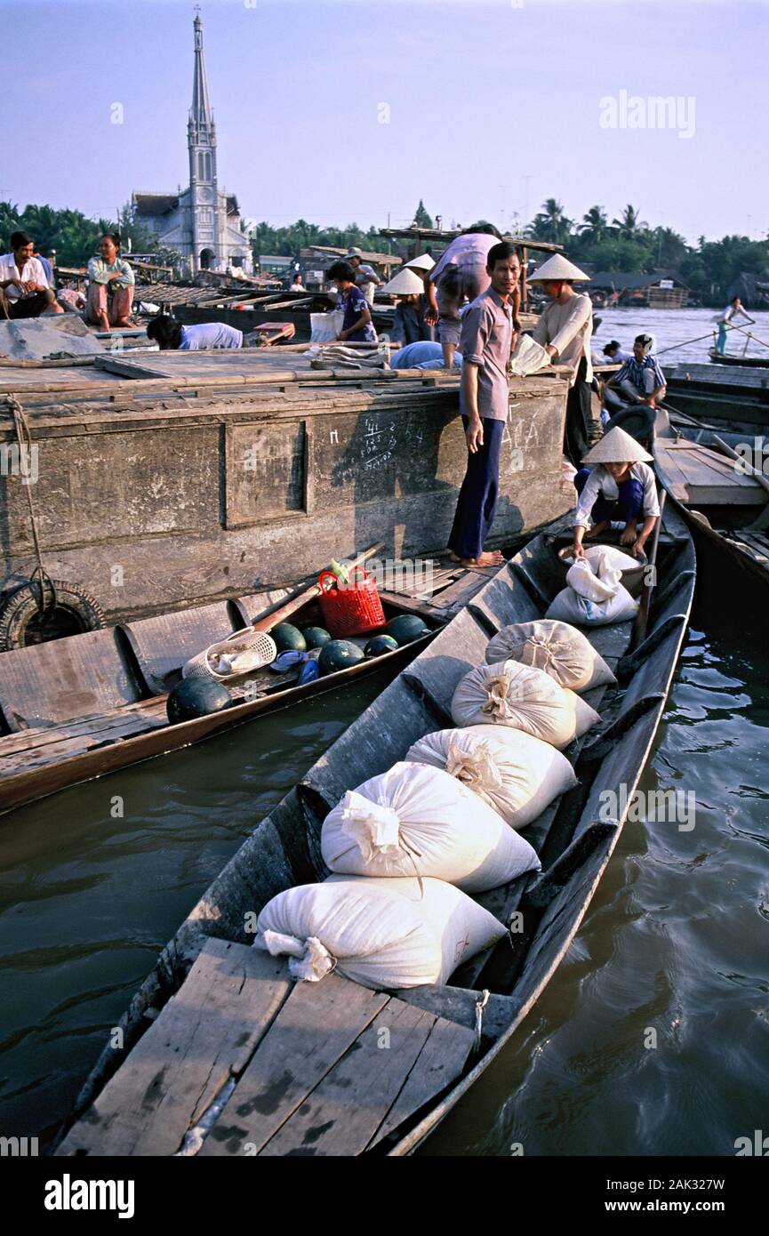 Vietnamese men loading sacks on a traditional wooden boat in the harbor ...