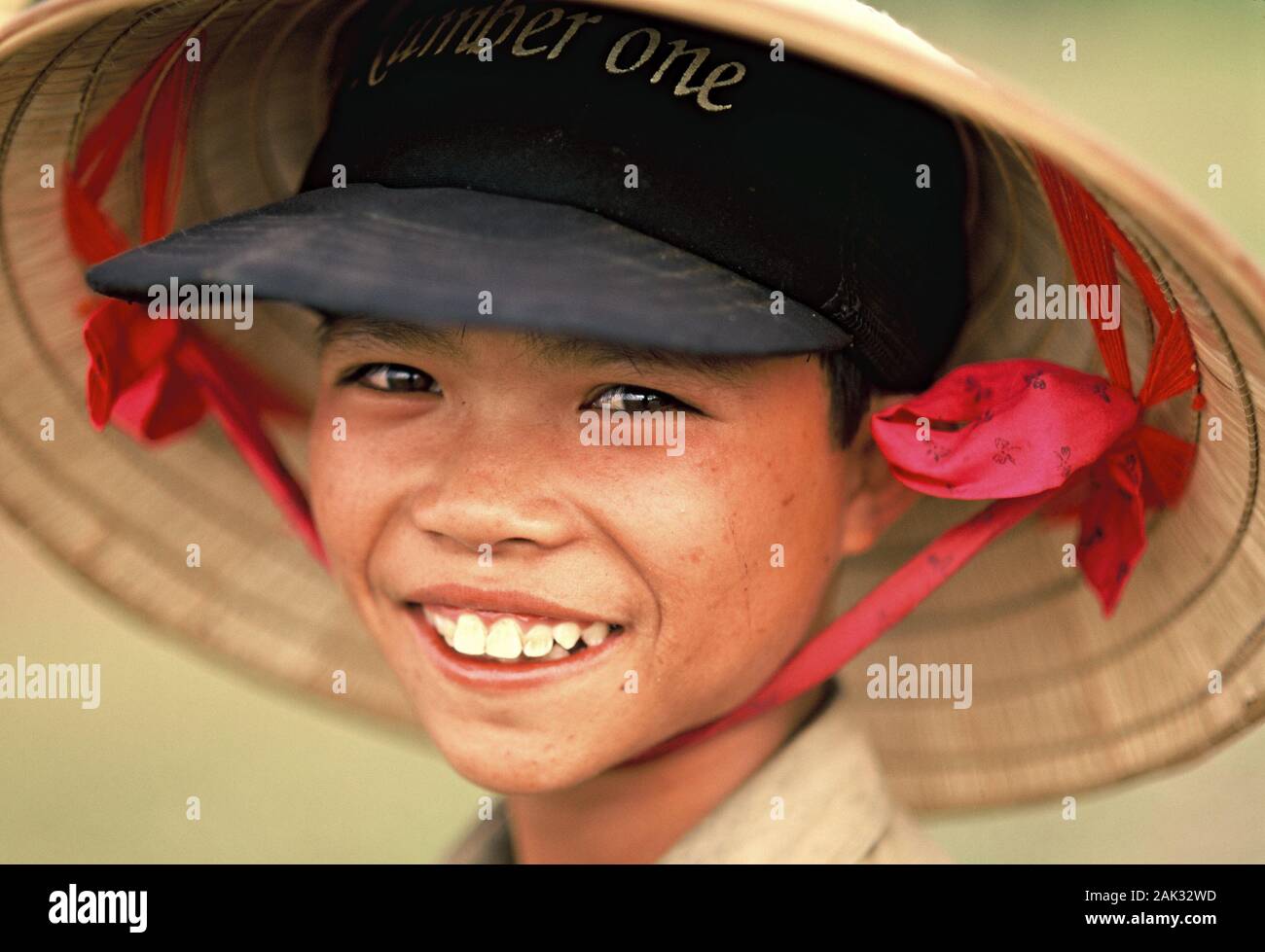 A Vietnamese boy who has covered his head both with a westerly peaked cap and a traditional ...