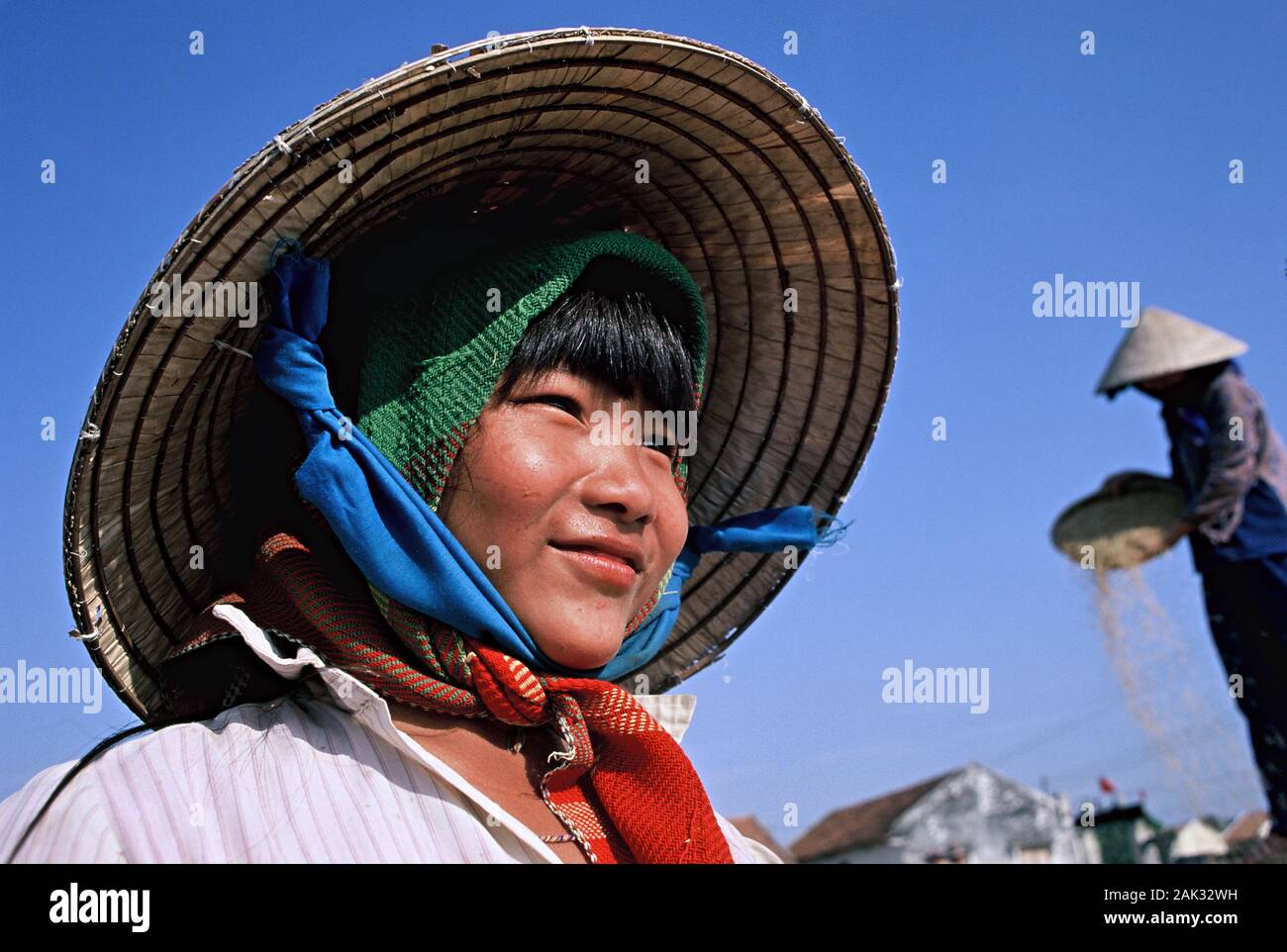 A young woman wearing a traditional straw hat stands on a market in her ...