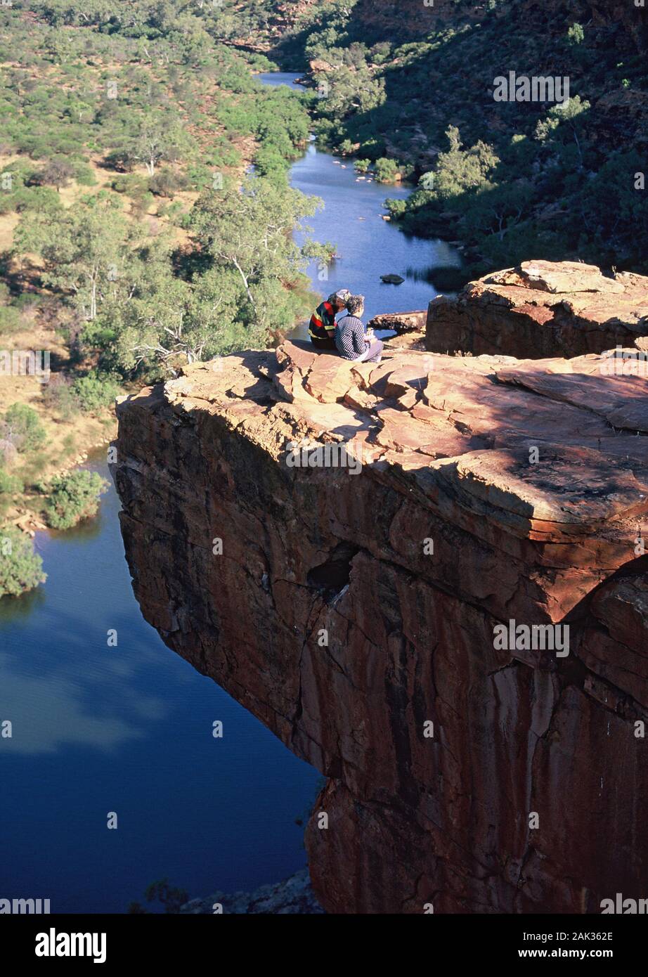 Two children are sitting on a steep sandstone cliff overlooking the ...