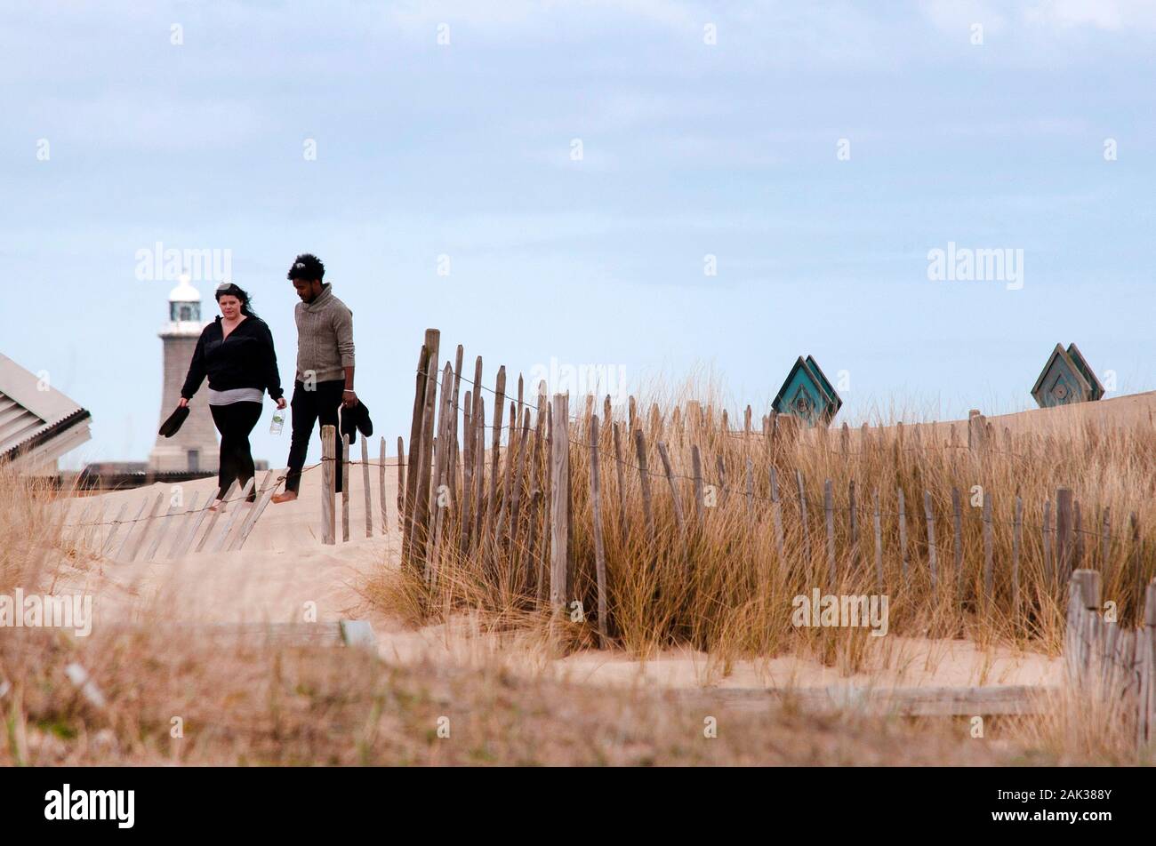 Couple walking past sand trap fencing,Sandhaven beach, South Shields ...
