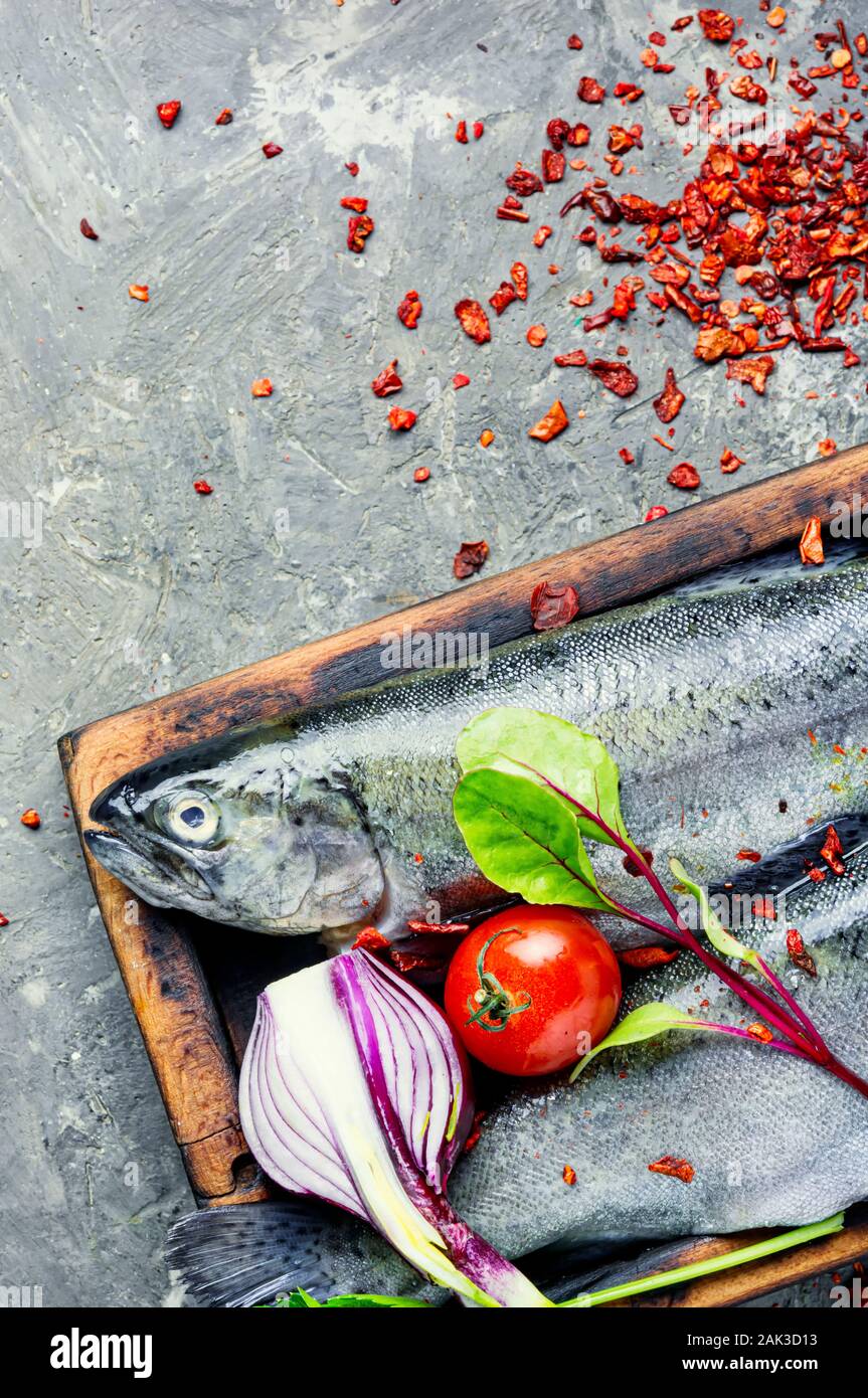 Fresh whole raw trout on a kitchen board.Fresh fish with vegetables and ...