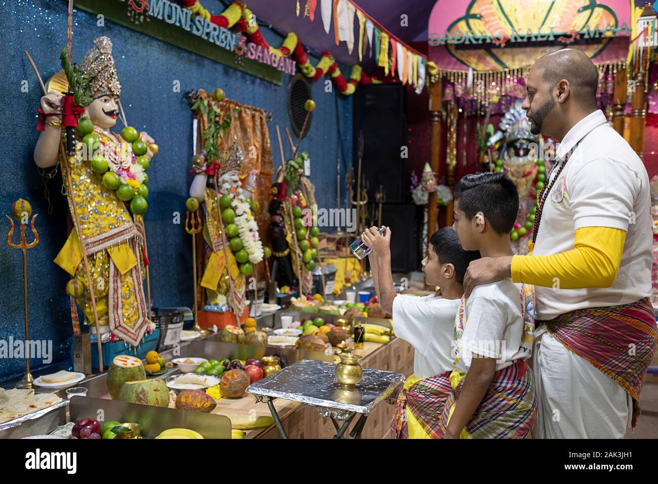 A father & his sons spray perfume at the deities to make a religious ...