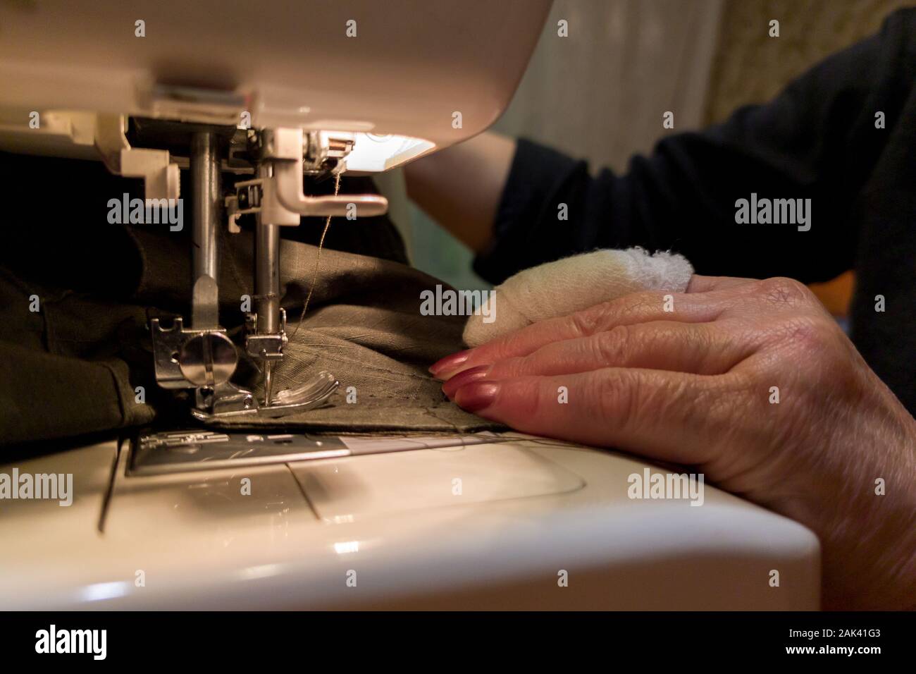a hand of aged womans with a bandaged finger sews with a sewing machine ...