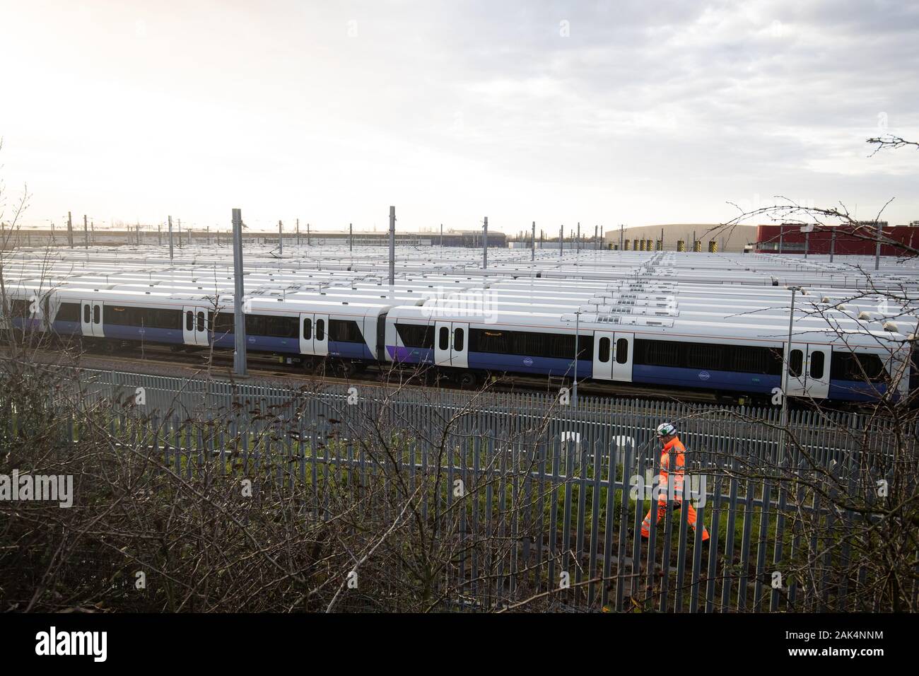 A worker wearing high visibility clothing passes Crossrail trains ...