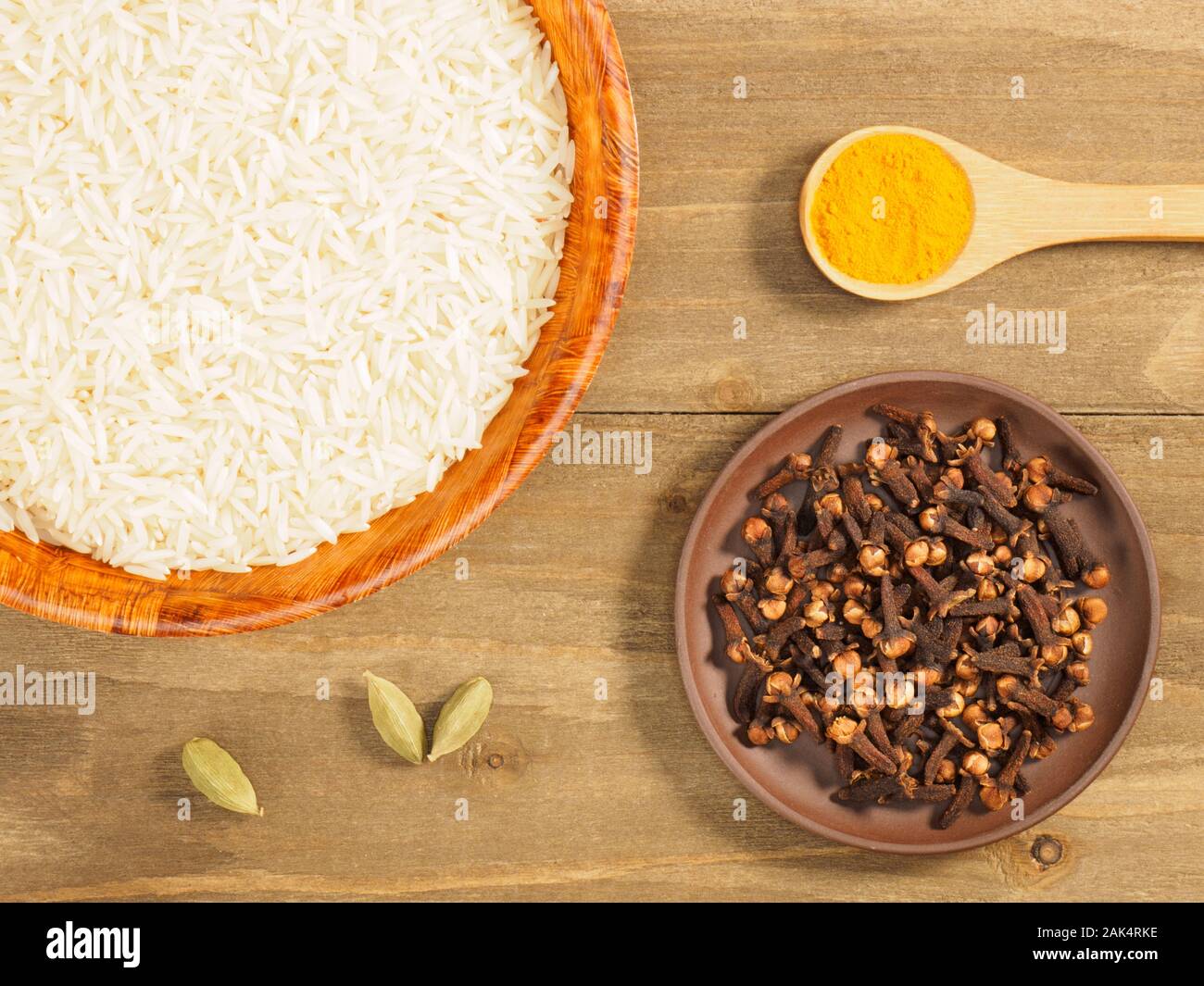 Rice, cloves, turmeric, green cardamom on brown wooden background ...