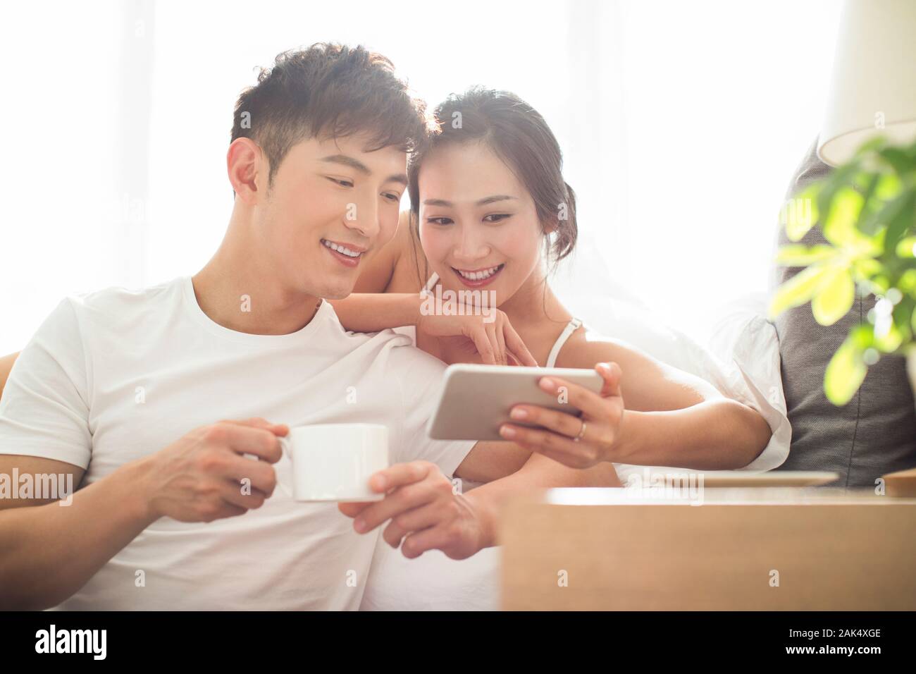 Happy young Chinese couple using smartphone in bedroom Stock Photo - Alamy