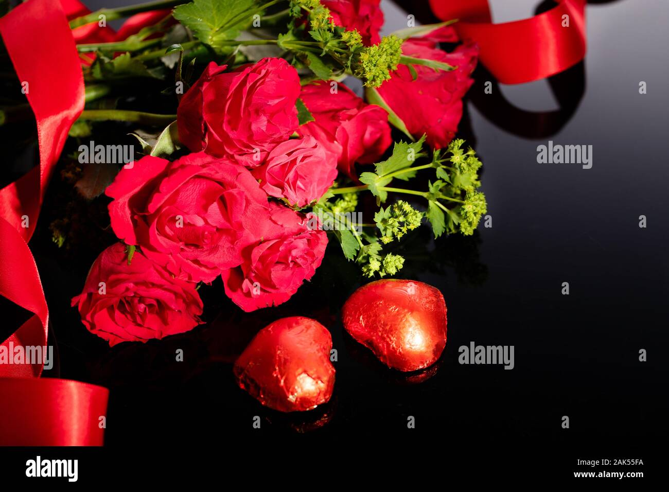 Red roses bouquet and heart-shaped chocolates, red ribbon on a black ...