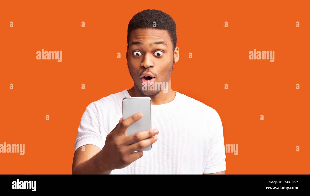 Shocking News. Anxious black man looking at phone seeing bad news or ...