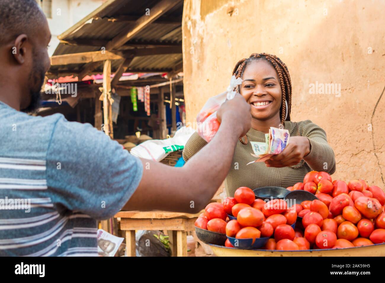 african girl selling tomatoes in a local african market to a male ...