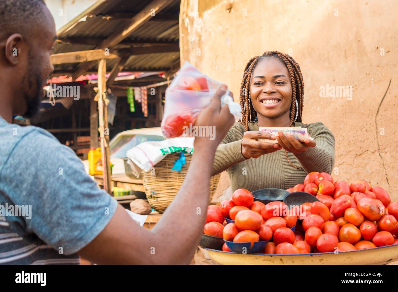 african girl selling tomatoes in a local african market to a male ...