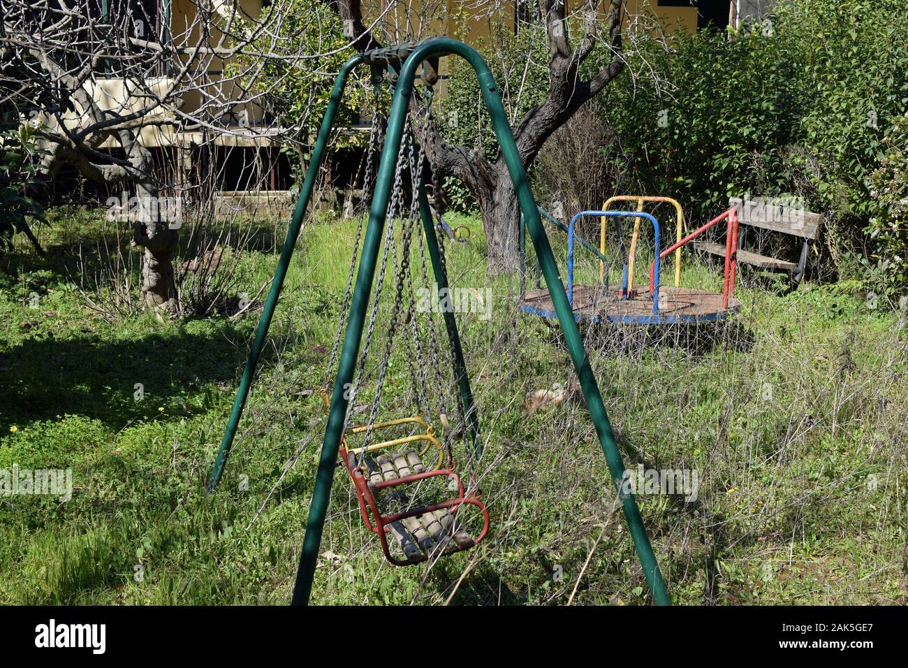 Old swings rusty merry-go-round and wooden bench in abandoned overgrown ...