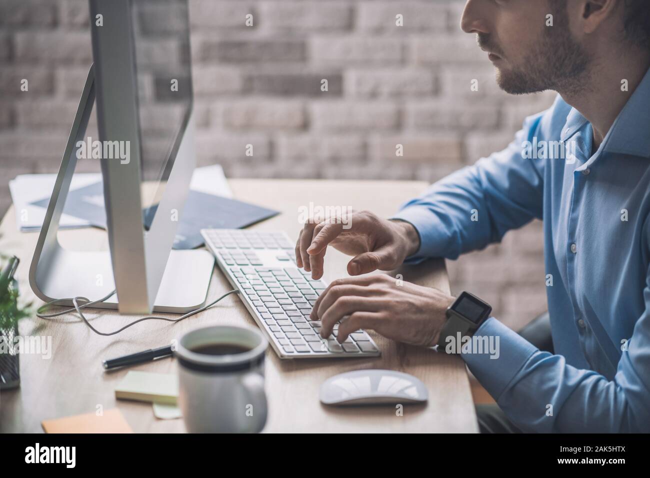 Typing. Young bearded man in blue shirt typing something Stock Photo ...