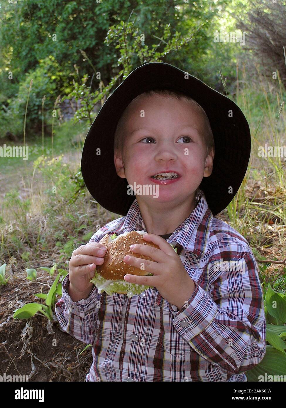 Boy eating hamburger in nature Stock Photo - Alamy