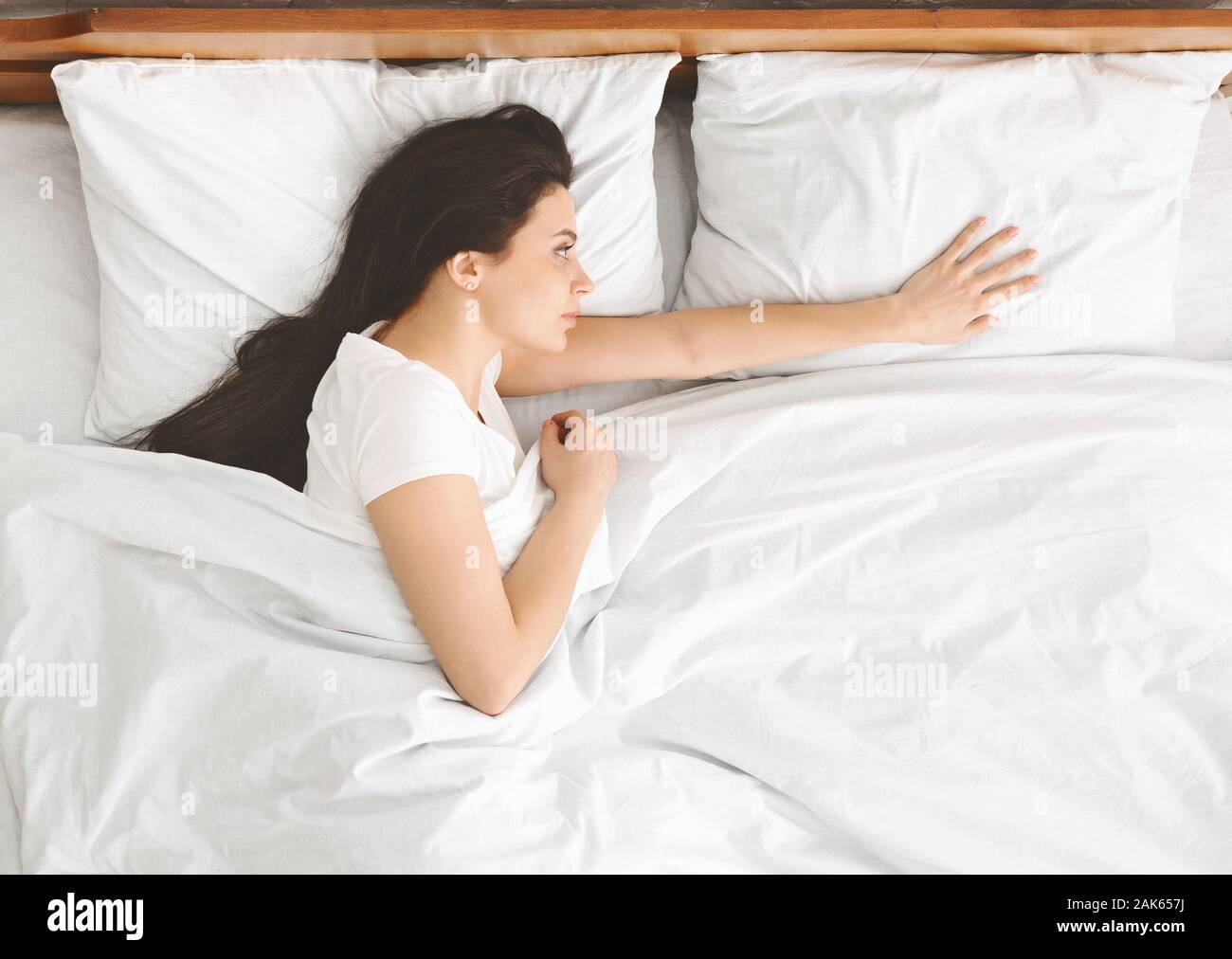 Loneliness. Young sad woman lying in double bed and looking on empty ...