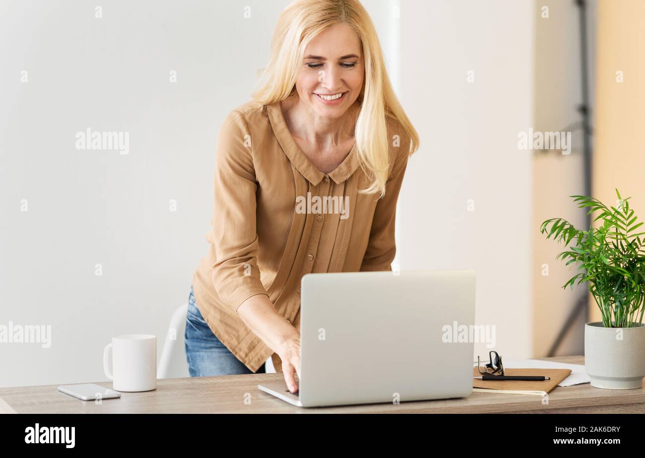 Business woman responding emails on laptop, standing near her desk in ...