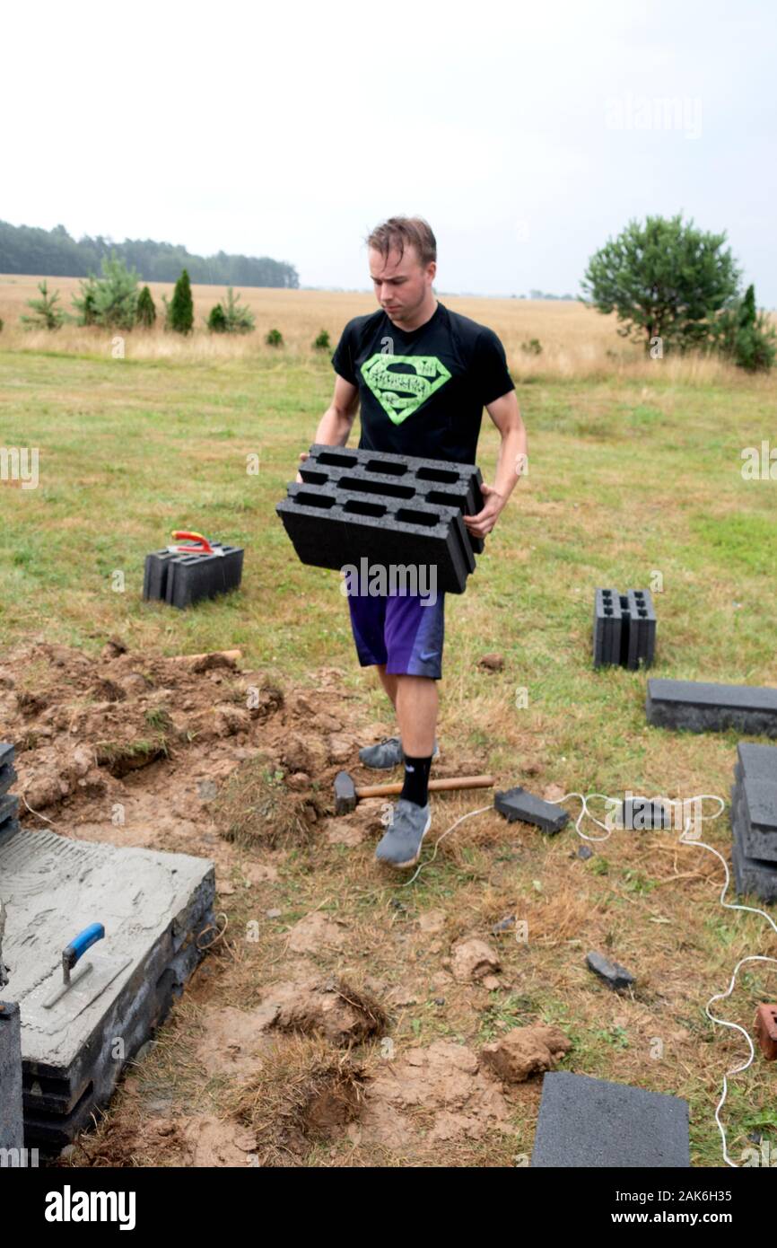 Older teen boy carrying a heavy brick for building an outdoor fireplace ...