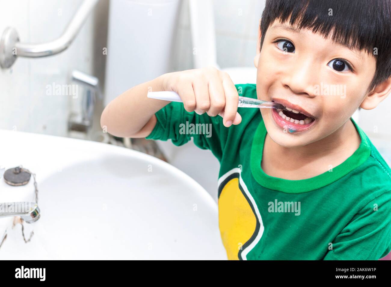 Little asian boy with toothbrush cleaning teeth in the bathroom. Close ...