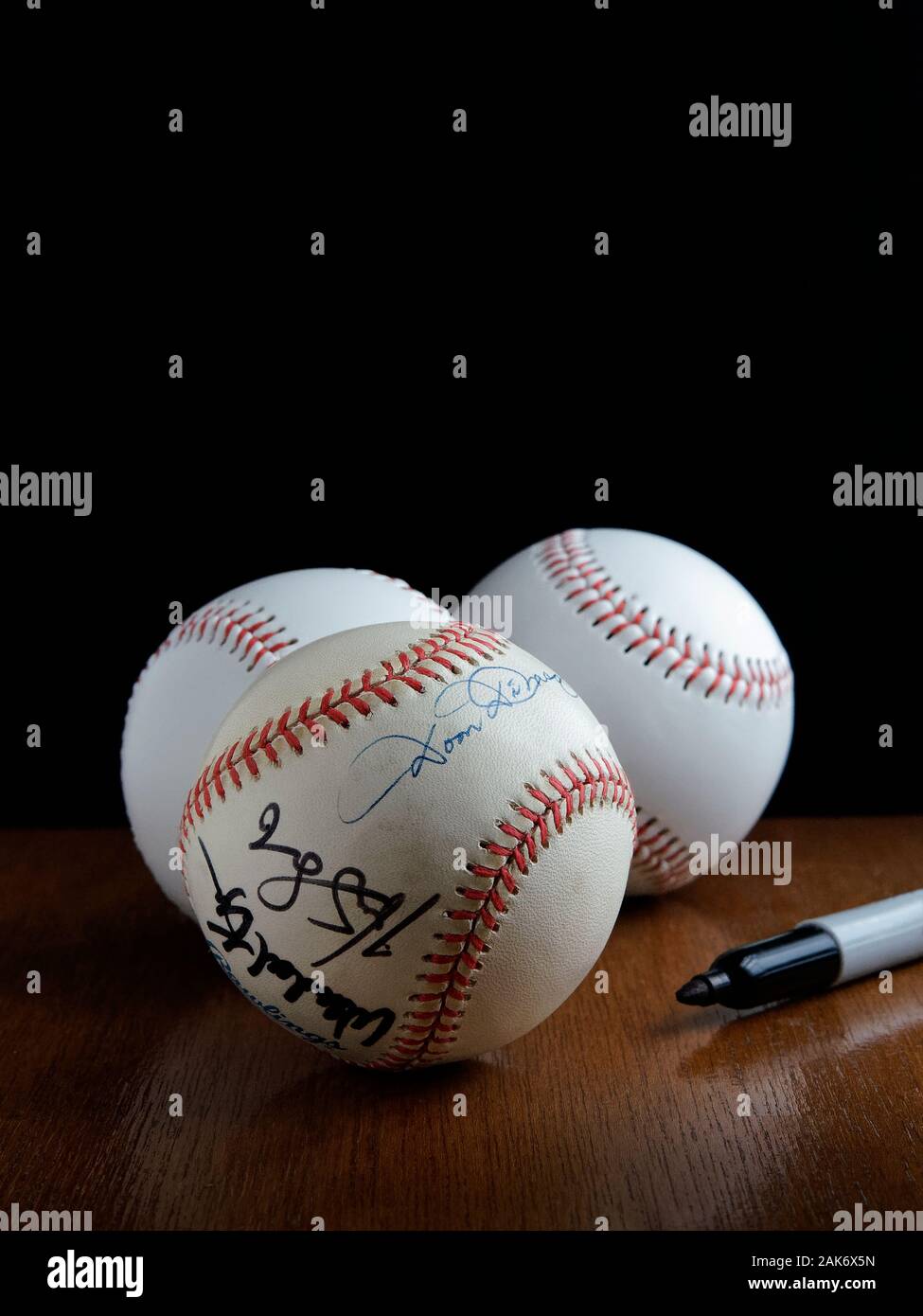 Three baseballs lined up on a wood table with an open maker to the ...