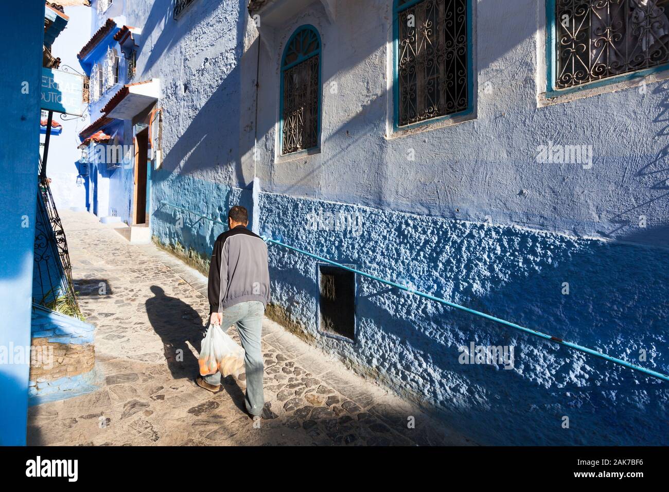 Man carrying plastic bags with oranges and bananas in the sunlit street ...