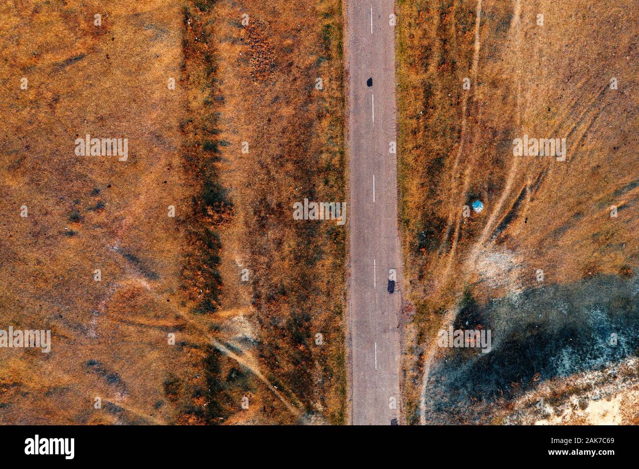 Top view of old worn road through grassy autumn meadow from drone pov ...