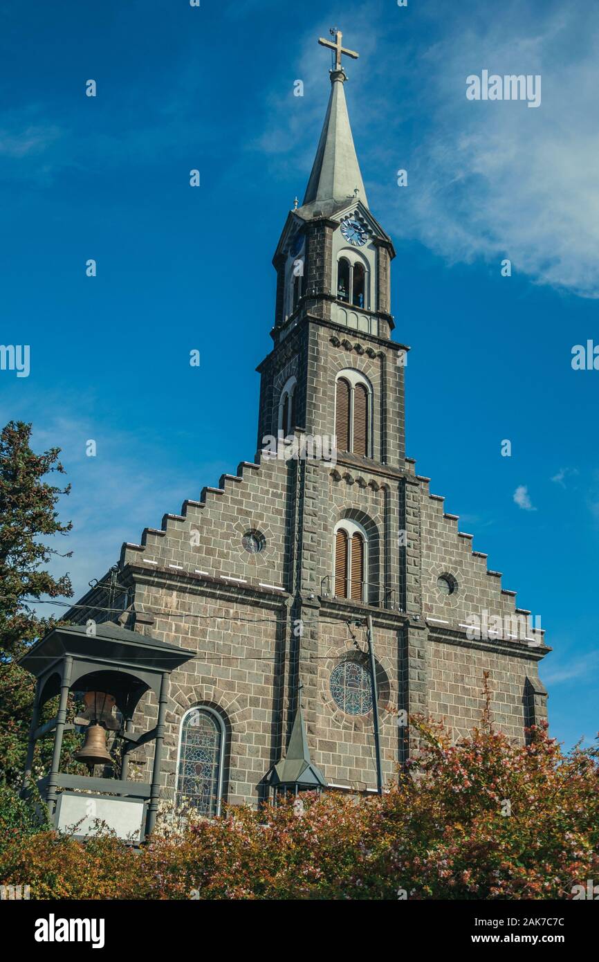 Church made of stone with steeple and bell in a garden at Gramado. A ...