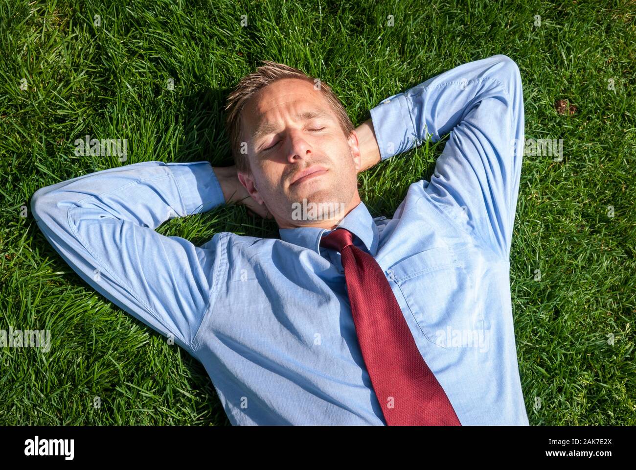 Tired businessman lying down outdoors taking a nap in bright green ...