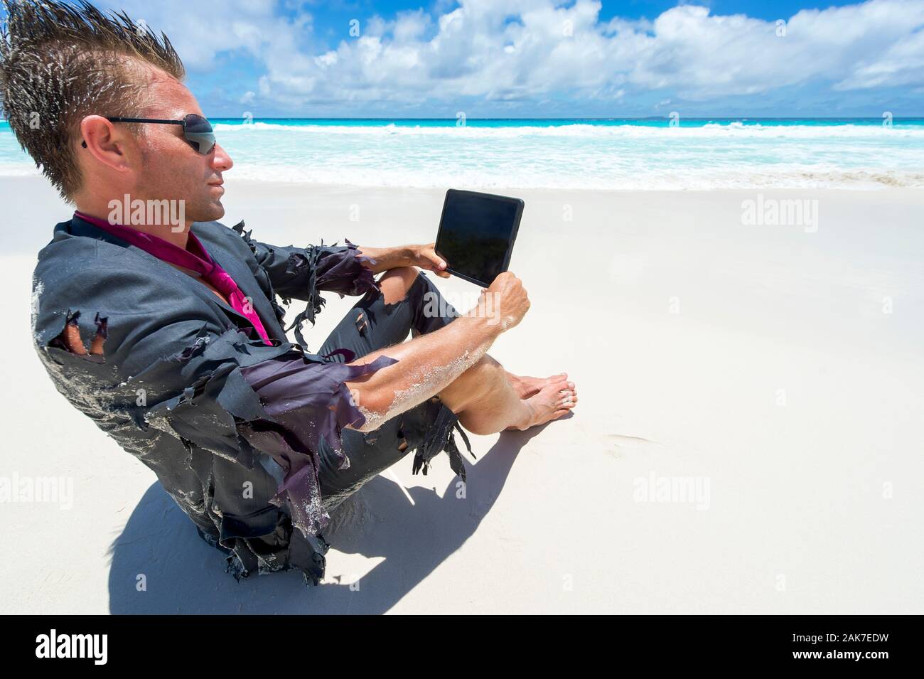 Castaway survivor businessman sitting on a tropical beach in a ragged ...