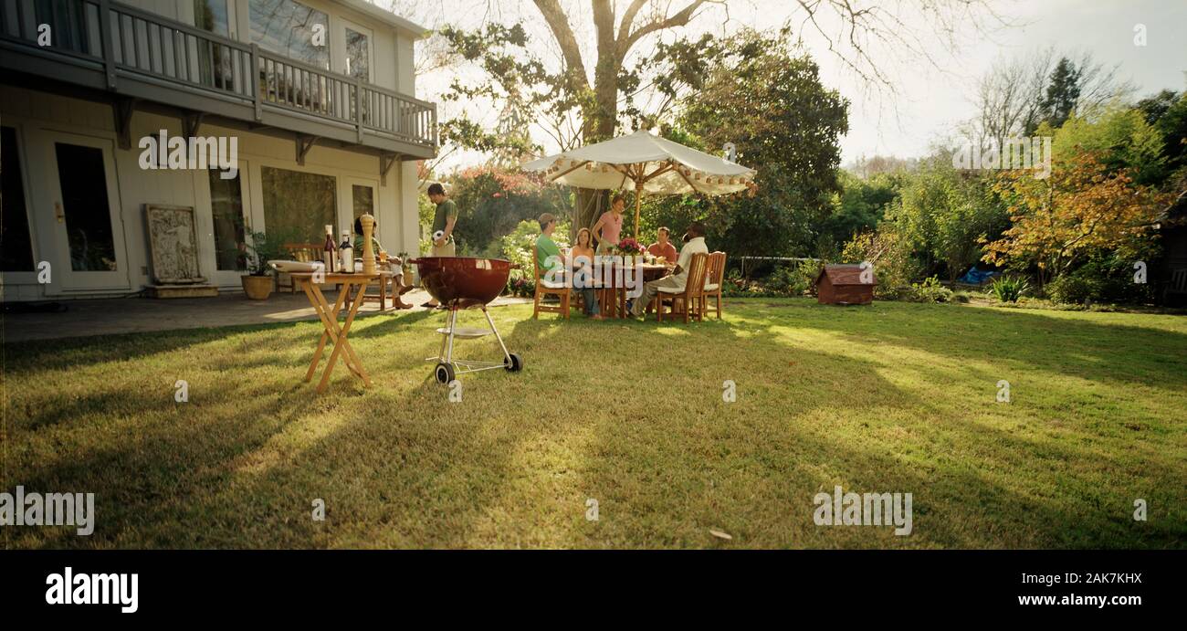 Family sitting around an outdoor dining table for a meal in the back ...