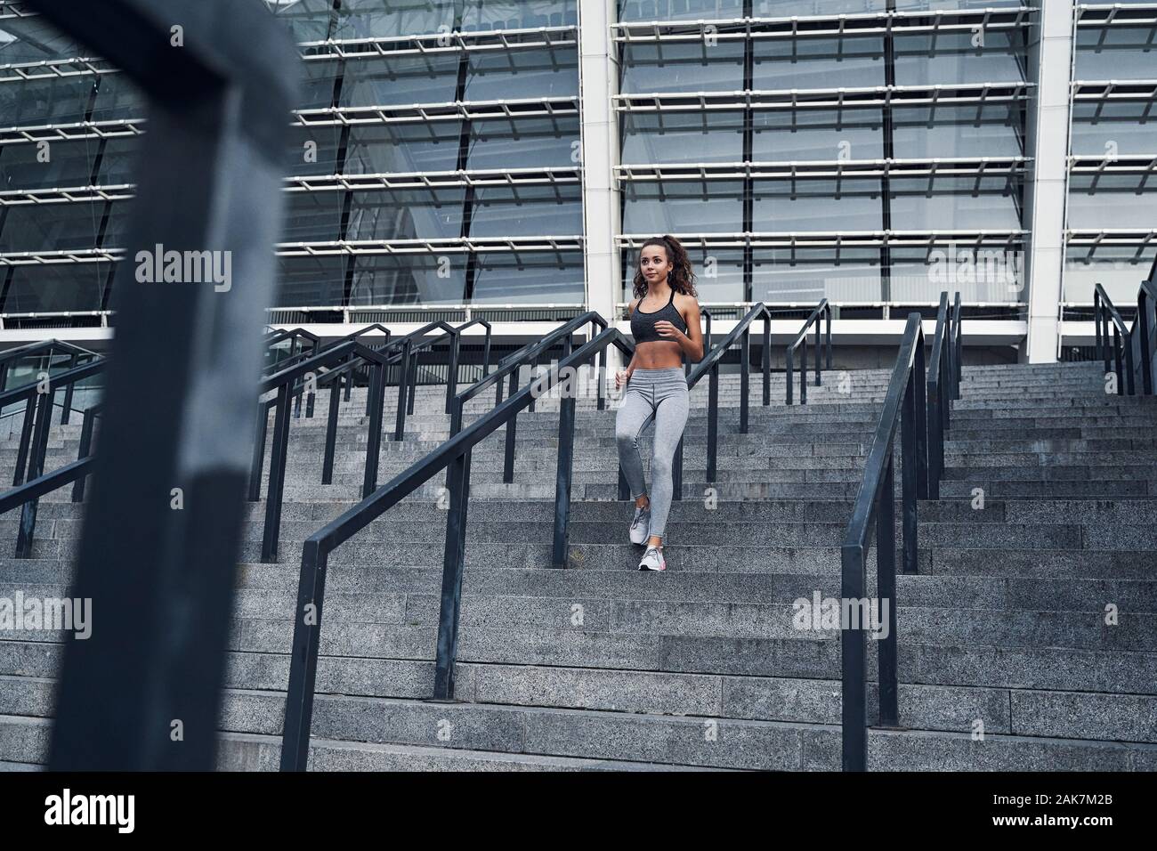Wide shot of young athletic woman running downstairs, training at urban ...