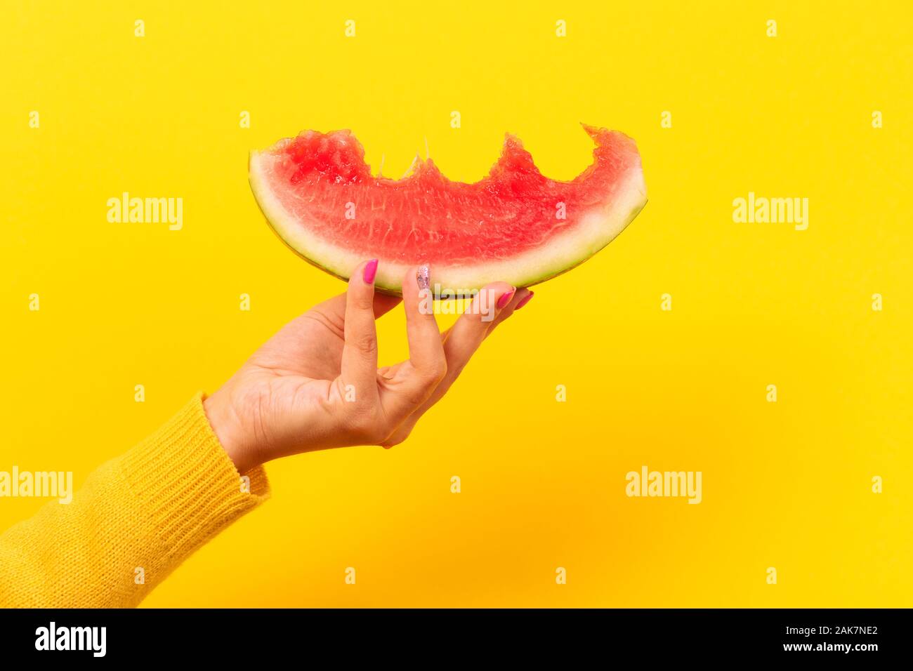 bitten watermelon slice in hand over yellow background. Summertime ...