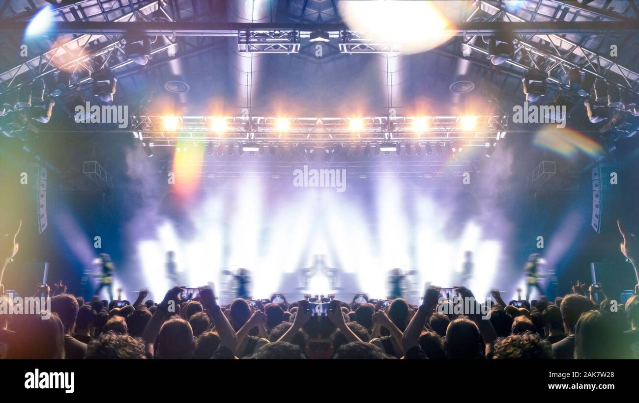 A shot taken in front of a concert stage lit in the night, people are ...