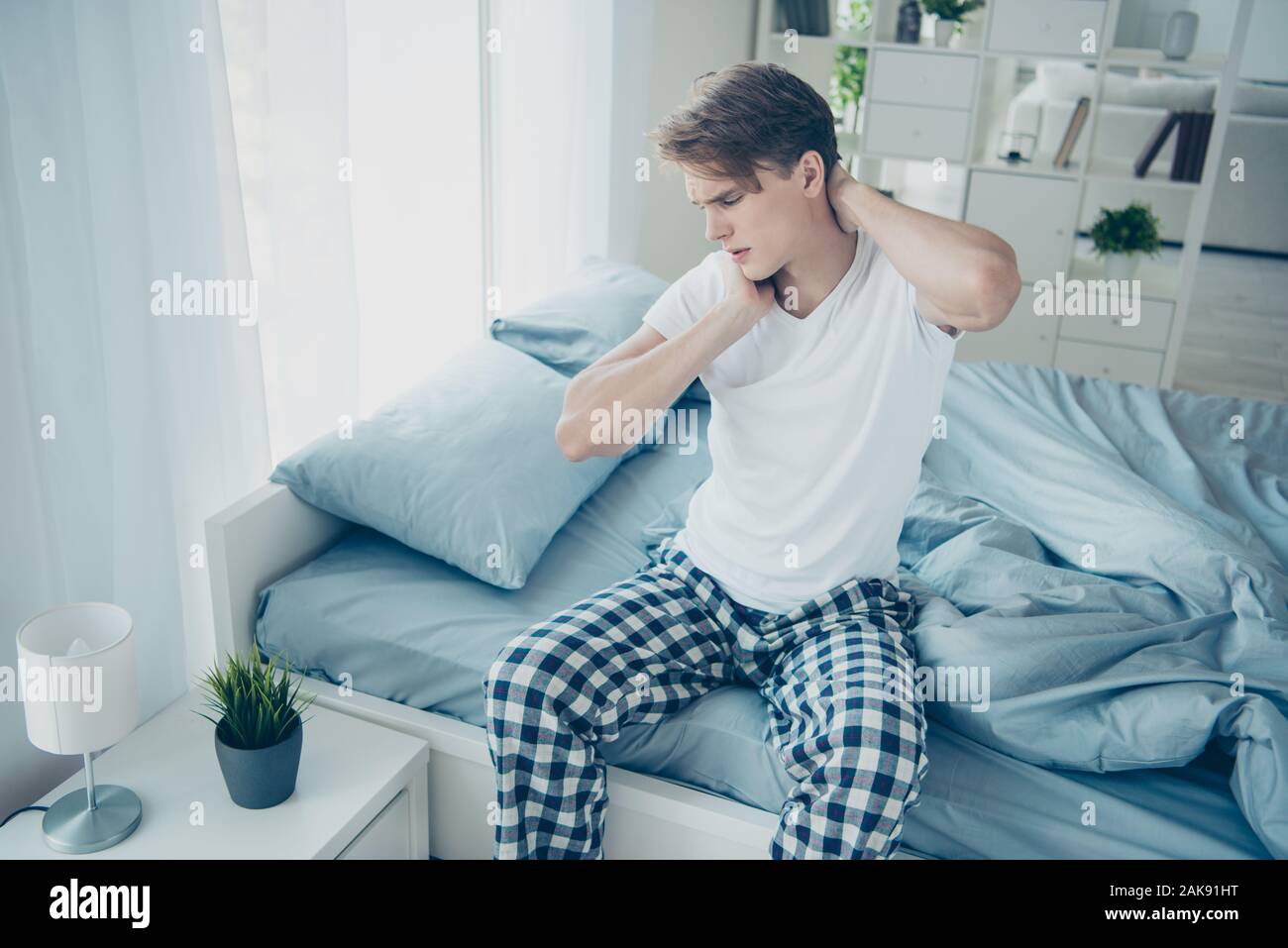 Portrait of upset sad man sit on bed wake up feel neck ache muscle ...