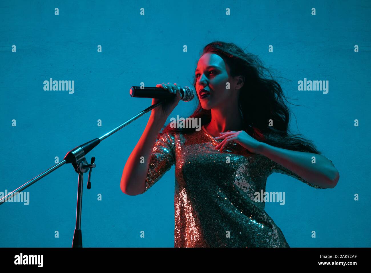 Caucasian female singer portrait isolated on blue studio background in ...