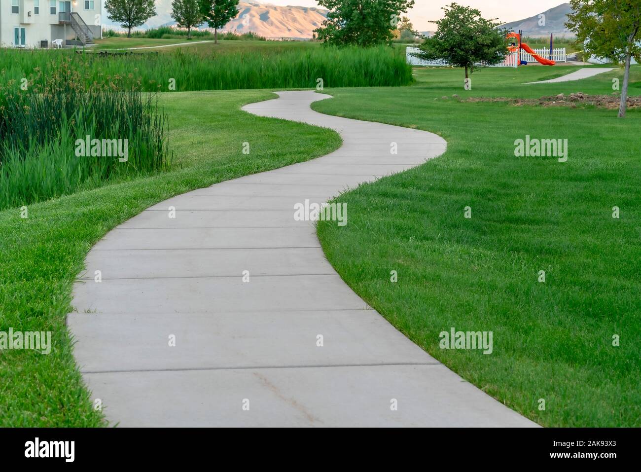 Narrow paved pathway winding through lush green grasses of park with ...