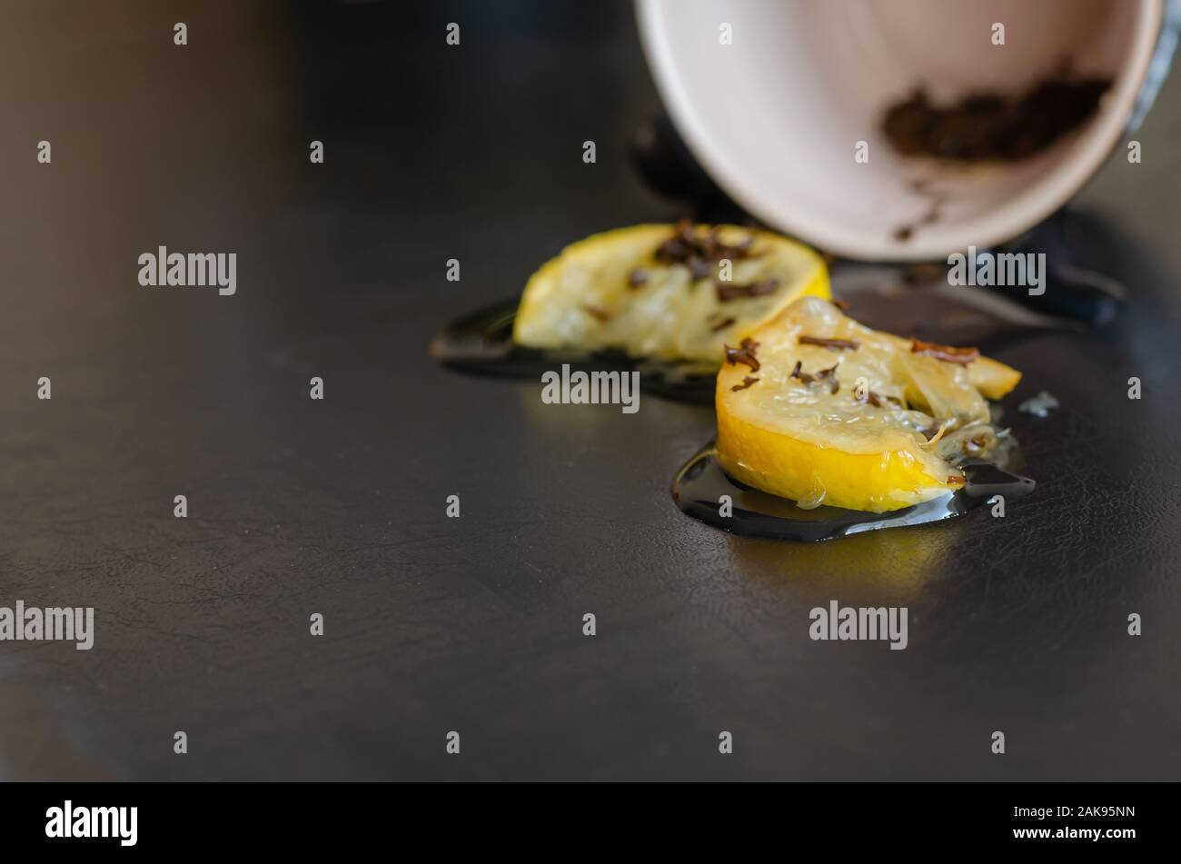 Dark table with a cup of spilled tea. Lemon slices and tea leaves with ...