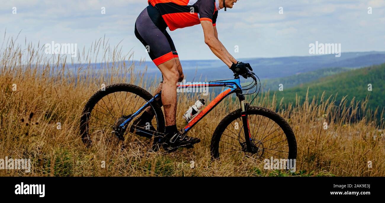 male cyclist downhill rides trail in dry grass. mud on feet and ...