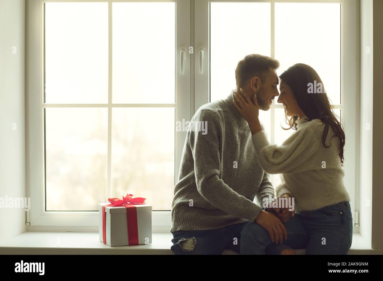 Rear view of a young couple sitting on a window sill by the window ...