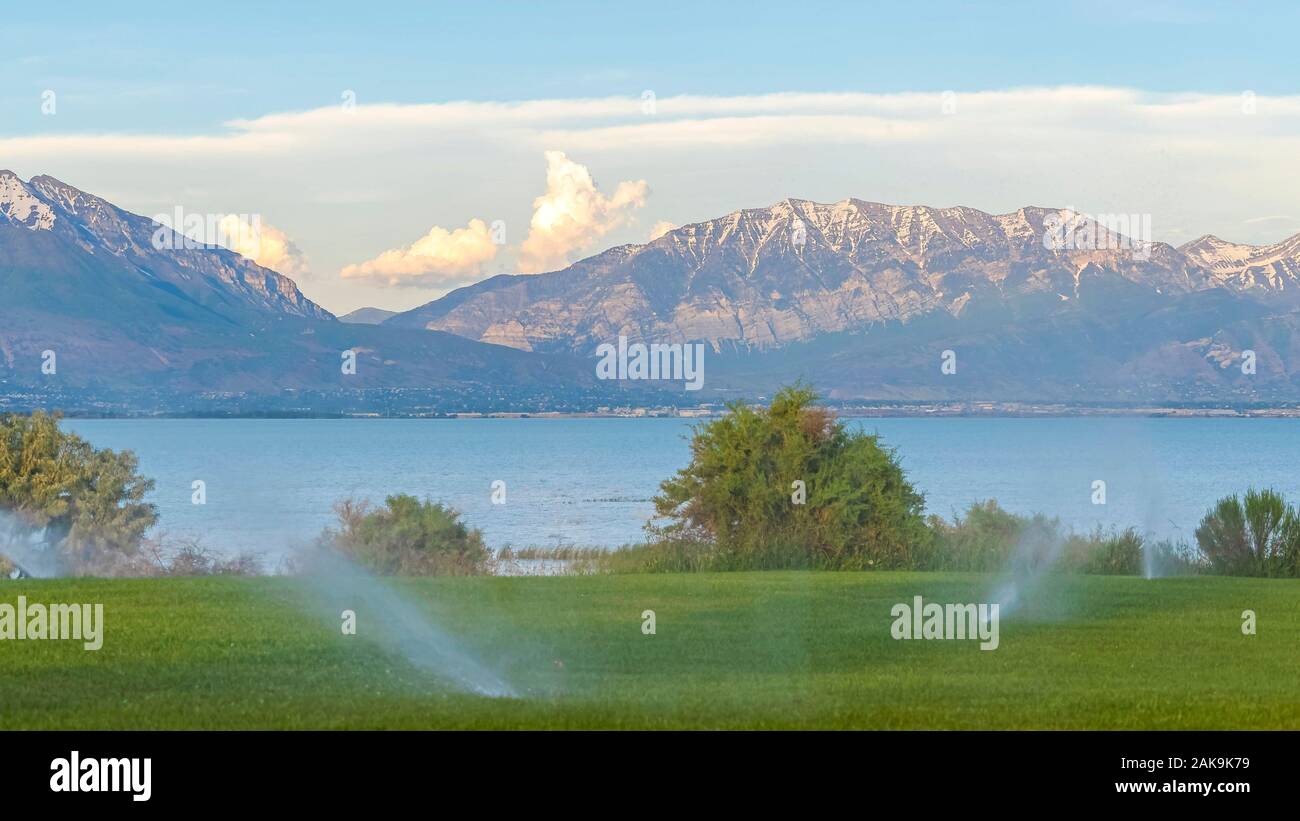 Pano frame Water from sprinklers on a green grassy land with scenic ...