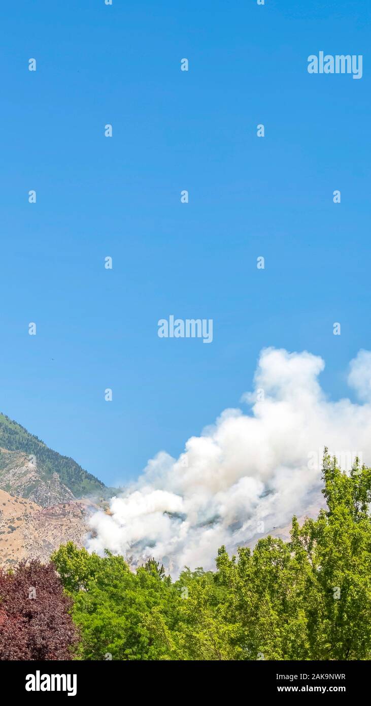 Vertical Fire in the mountain with smoke against slopes and clear blue ...
