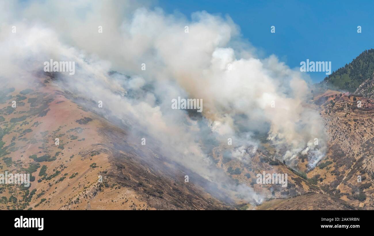 Pano frame Thick puffs of smoke from fire in the mountain against clear ...